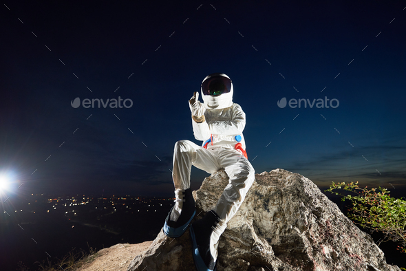 Spaceman sitting on rocky mountain and showing middle finger. Stock ...