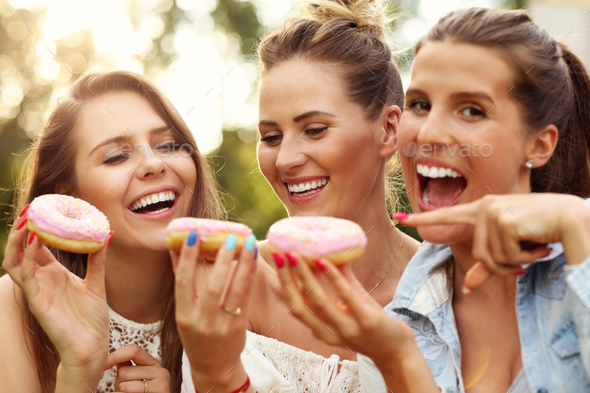 Happy group of friends eating donuts outdoors Stock Photo by macniak
