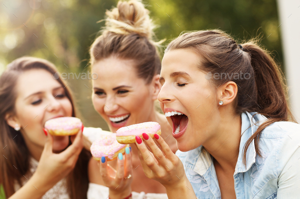 Happy group of friends eating donuts outdoors Stock Photo by macniak