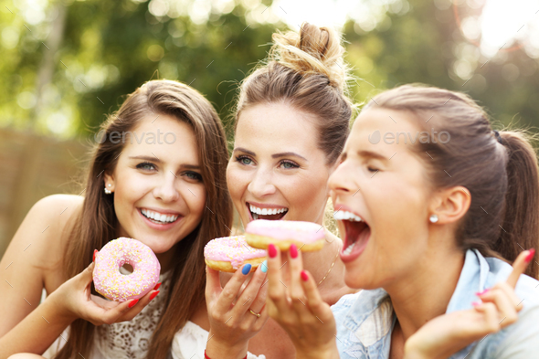 Happy group of friends eating donuts outdoors Stock Photo by macniak