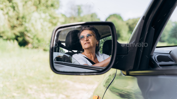 Senior cheerful smiling female driver behind wheel of car looking away ...