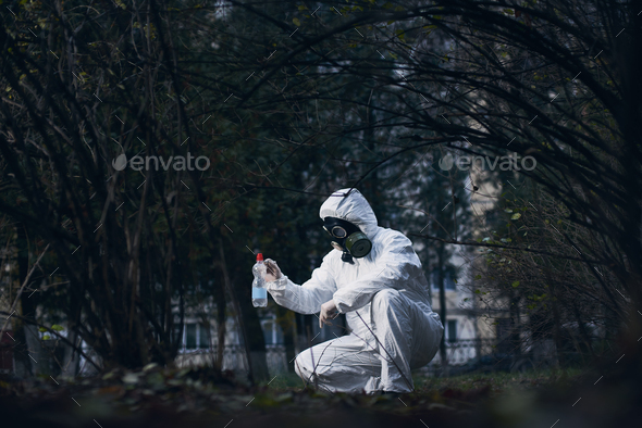 Scientist doing research outdoors, wearing white coverall and gas mask ...