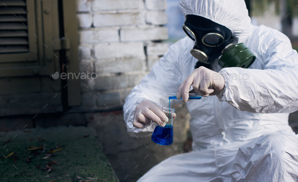 Scientist doing research outdoors, wearing white coverall and gas mask ...