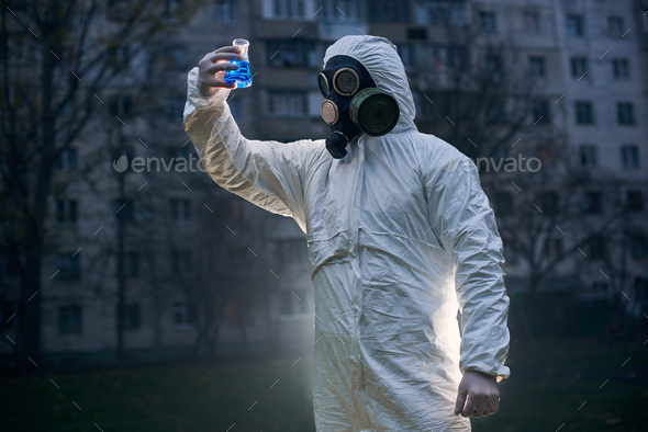 Scientist doing research outdoors, wearing white coverall and gas mask ...