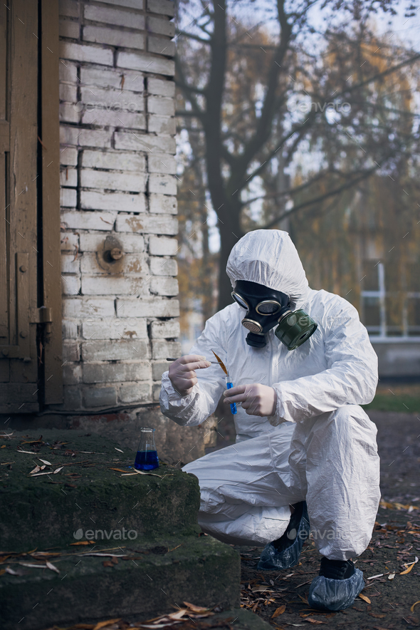 Scientist doing research outdoors, wearing white coverall and gas mask ...