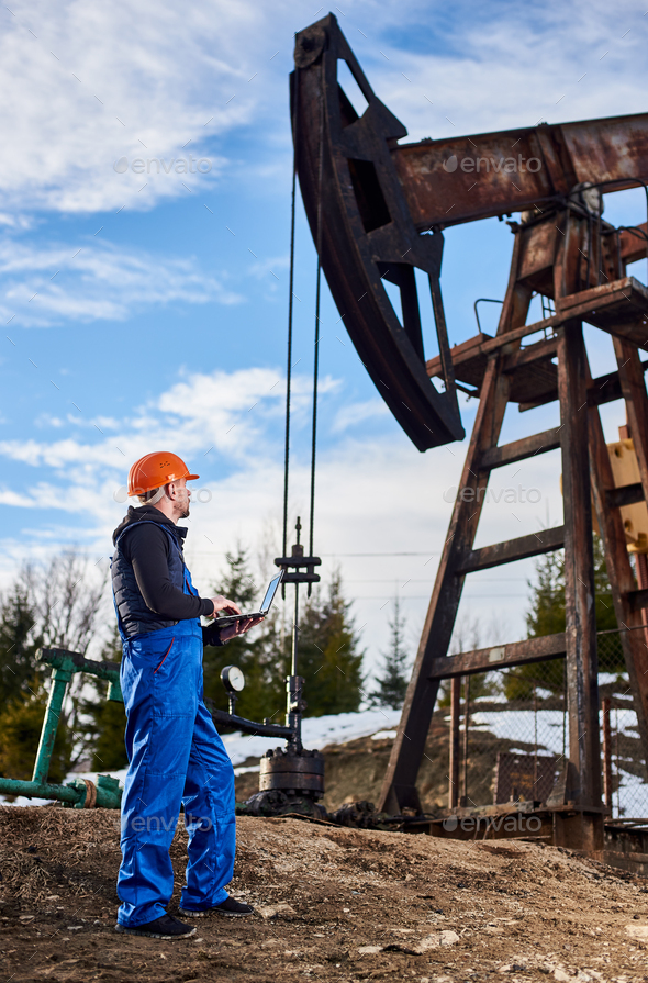 Petroleum engineer with laptop working in oil field. Stock Photo by ...