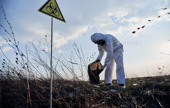 Researcher in protective suit collecting plastic garbage into black ...