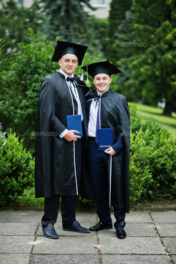 Two intelligent and handsome graduates in graduation gowns and caps ...