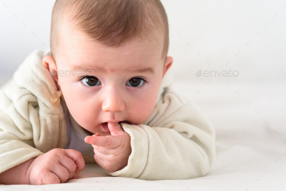 Portrait of an adorable smiling baby biting her own fingers putting her ...