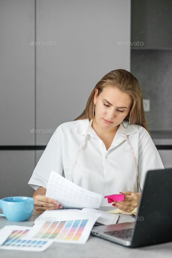 Woman sits at table in modern office next to color palette and fabric ...