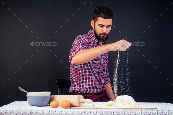 young and attractive caucasian man baker with beard makes the dough ...