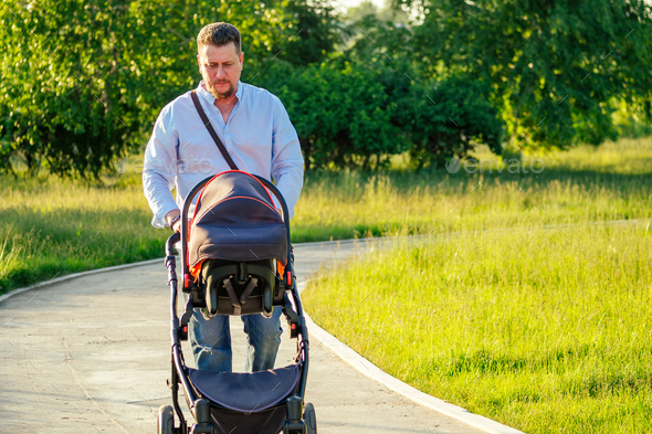 handsome man is walking with a baby in a stroller in the park Stock ...
