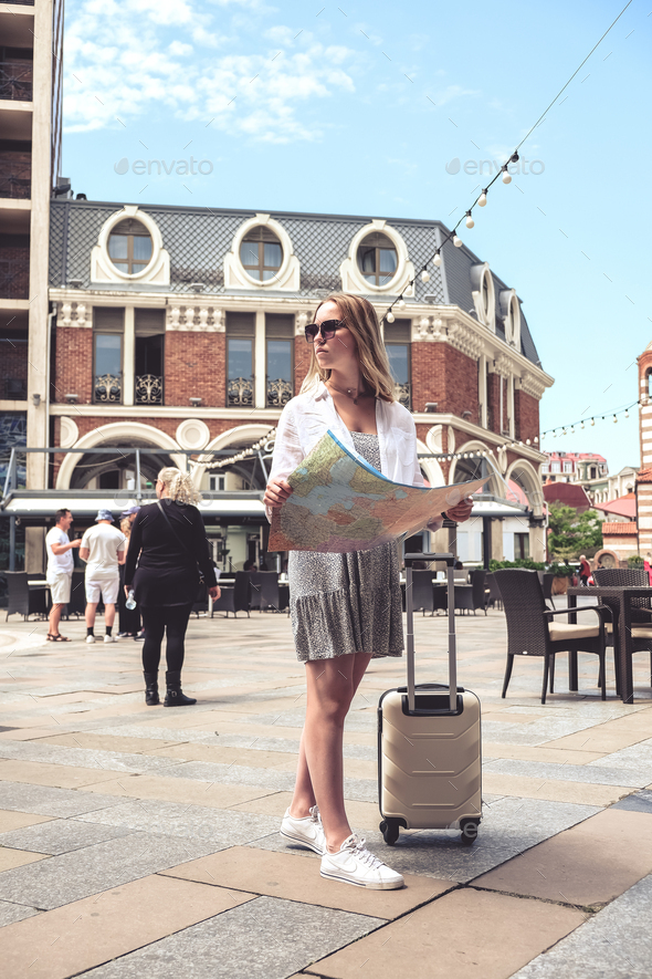Girl tourist traveler with a map and a suitcase in the old city.Travel ...