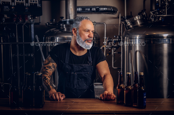 Old man posing at table with beer bottles inside brewery Stock Photo by ...