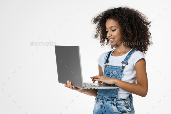 Portrait of smiling little girl using laptop computer while standing ...