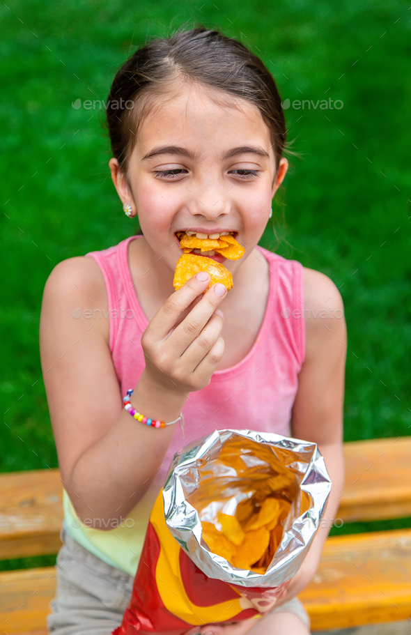 The child eats chips in the park. Selective focus. Stock Photo by yanadjana
