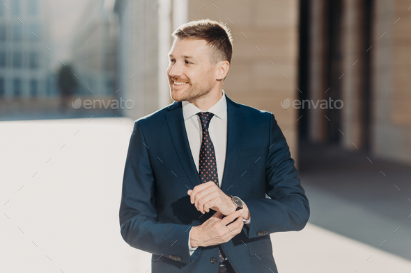 Delighted male CEO wears elegant formal suit, stands outdoor on street ...