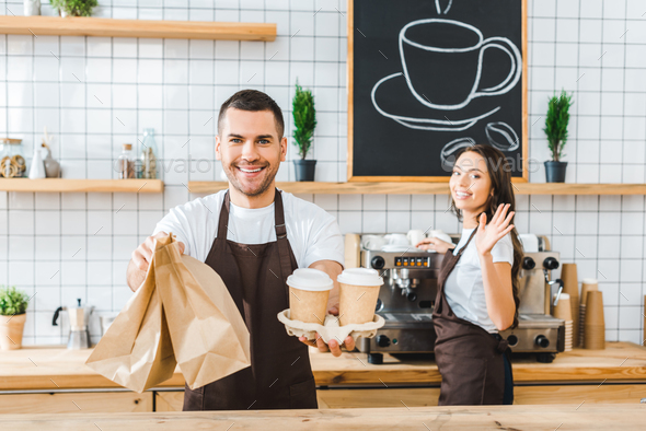 handsome cashier holding paper cups and bags wile attractive brunette ...