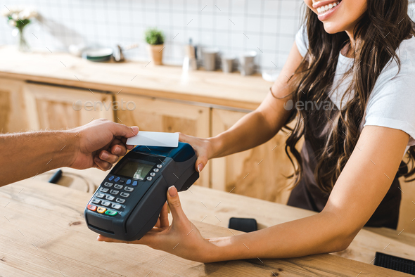 cropped view of cashier standing near bar counter in brown apron and ...