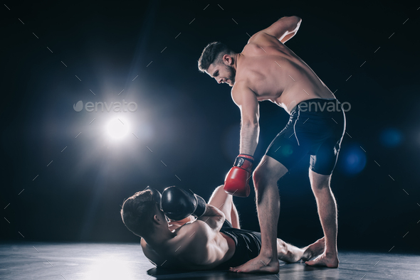shirtless strong mma fighter in boxing gloves standing above opponent ...