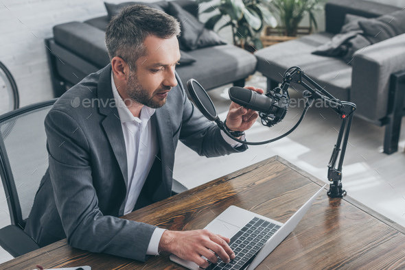 handsome radio host adjusting microphone and using laptop in radio ...