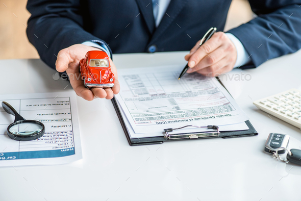 partial view of man in formal wear holding red toy car and signing ...