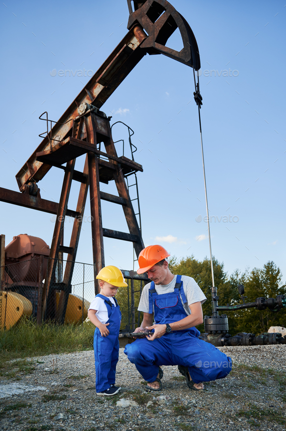 Oilman showing to child wrench on the background of oil rig. Stock ...