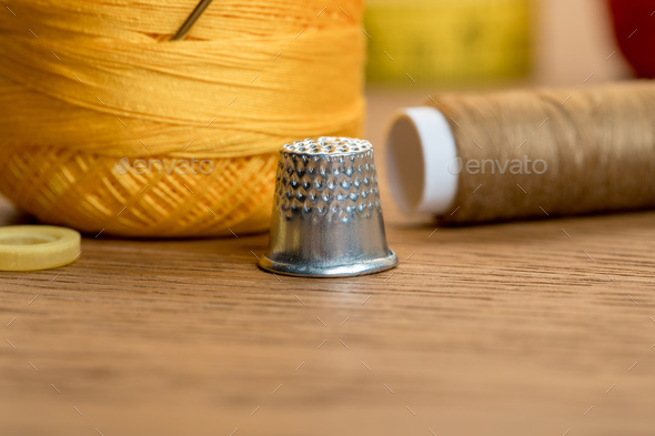 close up view of thimble with yarn ball and thread coil on wooden table ...