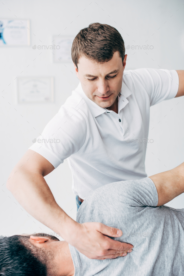 handsome chiropractor stretching arm of handsome patient in hospital ...