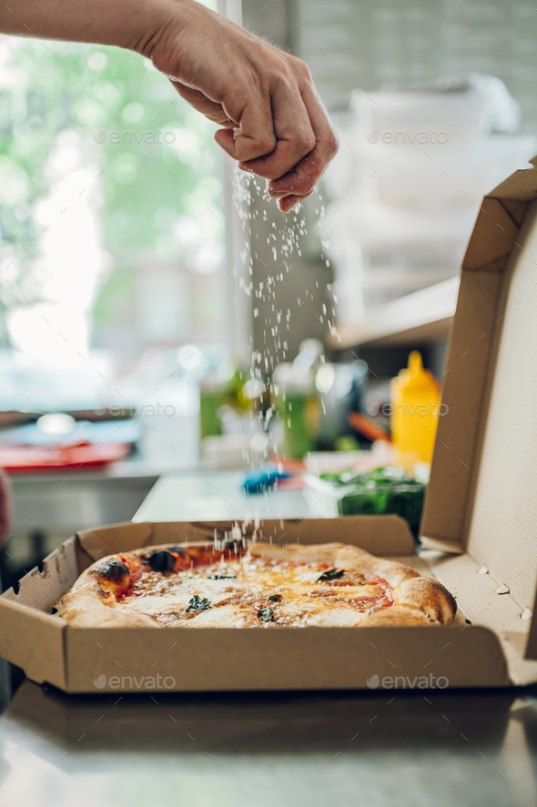 Man worker in a pizza place sprinkling cheese over a baked pizza Stock ...