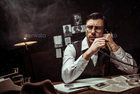 Pensive detective in glasses talking on telephone in dark office Stock ...