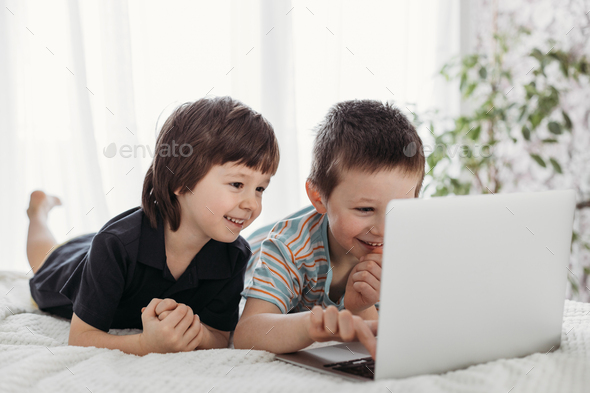 The boys are watching something on the computer while lying on the bed ...