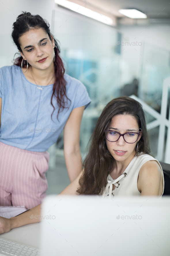 Two young women watching messages on computer screen at work Stock ...