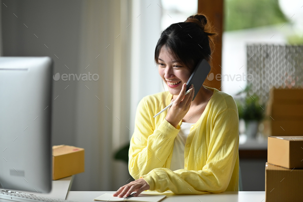 Smiling female small business owner using computer and talking on ...