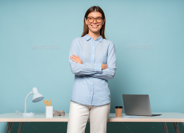 Smiling pensive female CEO in business spectacles standing near table ...