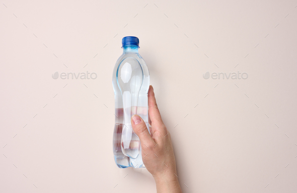 Female hand holds a plastic transparent bottle on a beige background ...
