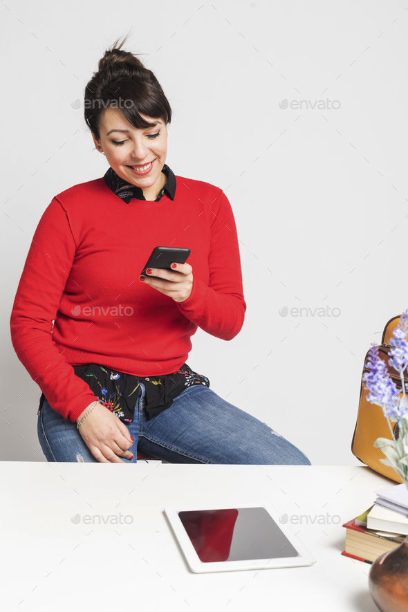 woman sitting on a stool while using a mobile phone at office against ...