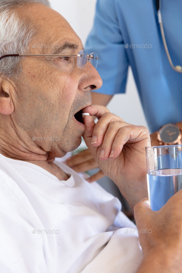 Caucasian senior man eating medical pills lying on the bed at home ...