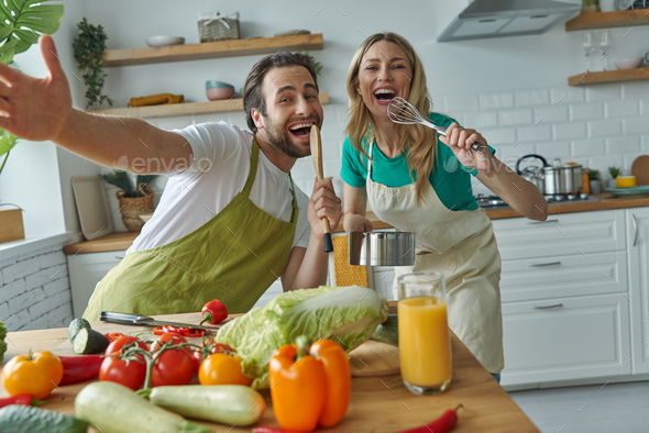 Playful young couple singing while cooking together at the kitchen ...