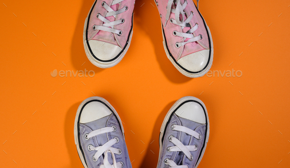 Two pairs of textile sneakers on an orange background stand opposite ...