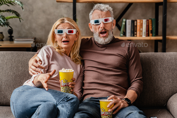 Excitement couple in 3d glasses holding buckets with popcorn watching movie on sofa Stock Photo ...