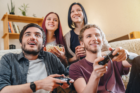 Multiethnic joyful group of young people playing games on console while ...