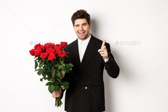 Image of handsome romantic guy in black suit, holding bouquet of roses ...