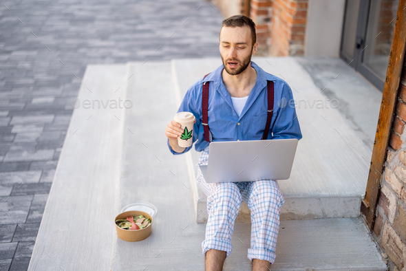 Stylish guy works on laptop computer on a street Stock Photo by RossHelen