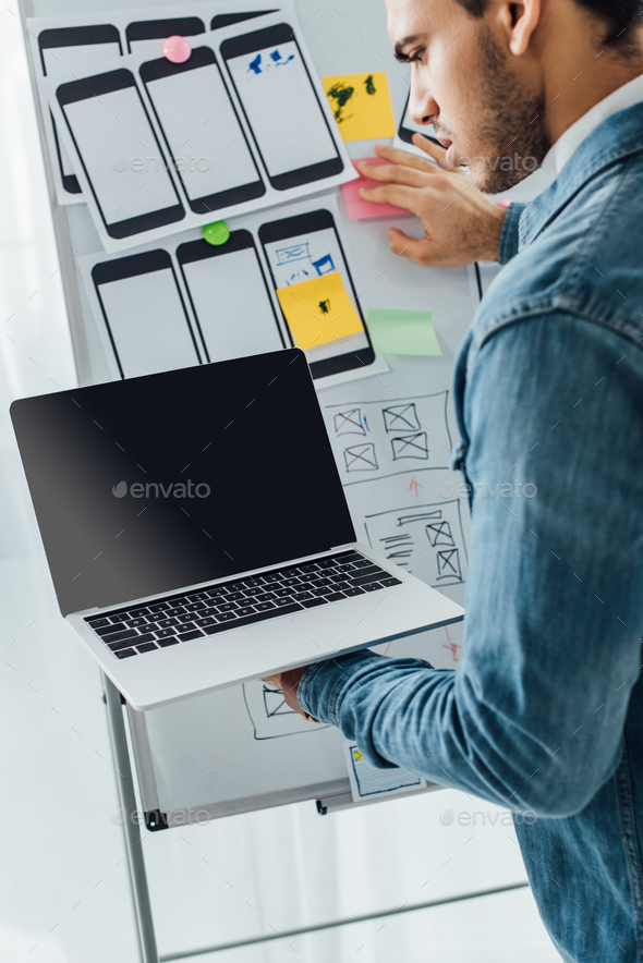 Ux designer using laptop near website templates on whiteboard in office ...