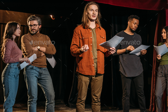 multicultural actors and actresses rehearsing with scripts on stage in ...