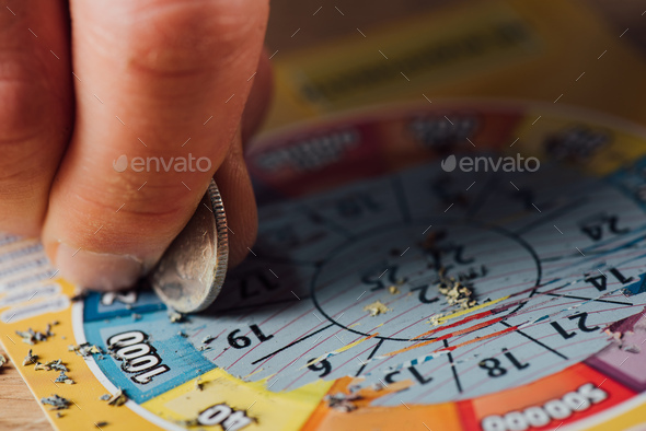 cropped view of gambler scratching lottery ticket with silver coin ...