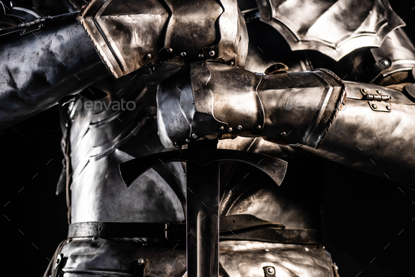 cropped view of knight in armor holding sword isolated on black Stock ...