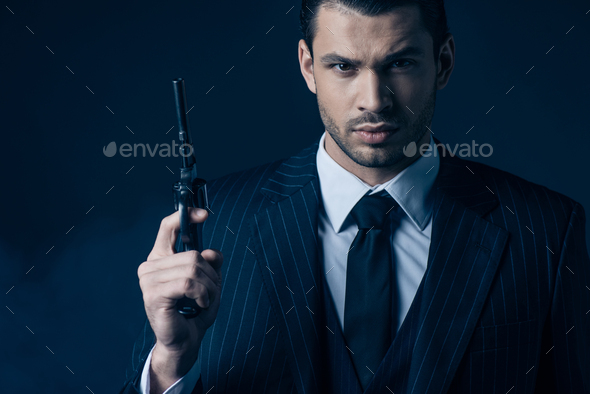 Front view of gangster holding gun and looking at camera on dark blue ...