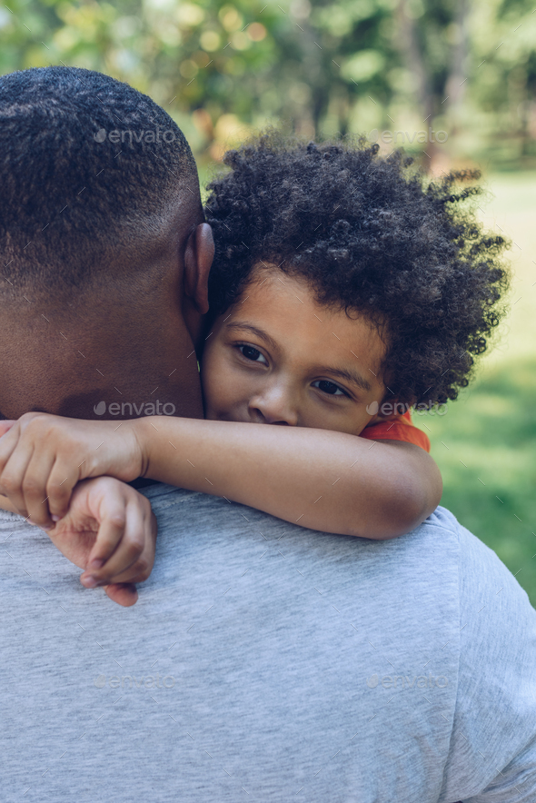 adorable african american boy hugging father while walking in park ...